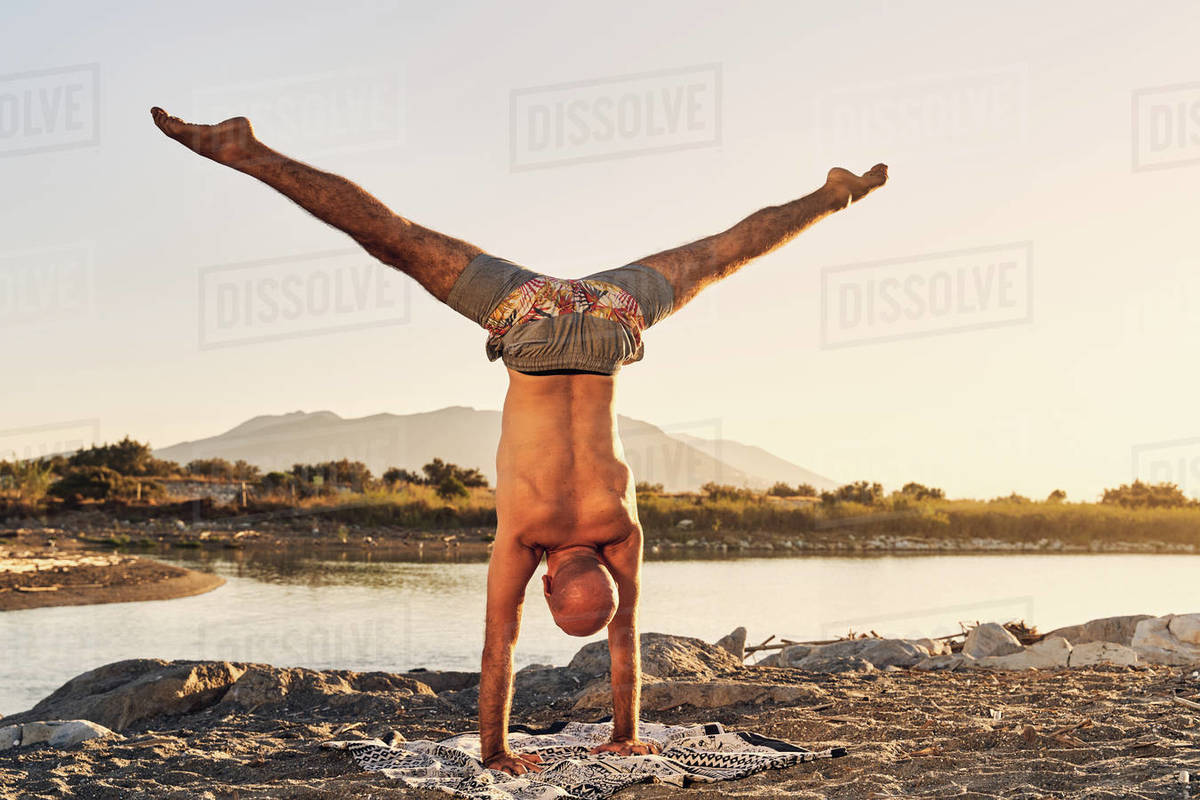 Back view of shirtless male balancing in Handstand pose while ...