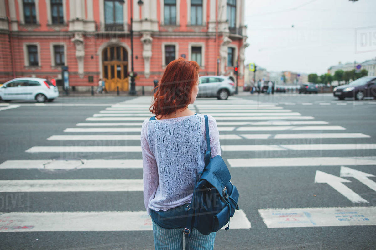 Back view of anonymous female with red hair standing near crosswalk in ...