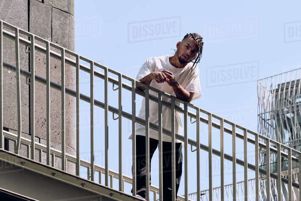 Young African American man leaning on railing of bridge while spending ...