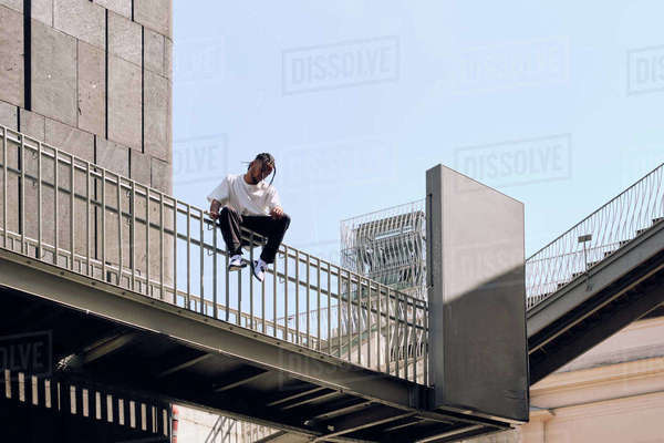 Young African American man sitting on railing of bridge while spending ...
