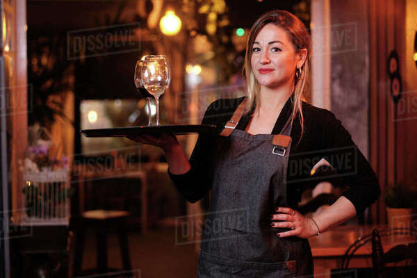 Confident adult hostess smiling and holding tray with two goblets of ...