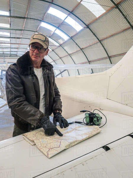 Pilot with map beside small plane - Stock Photo - Dissolve