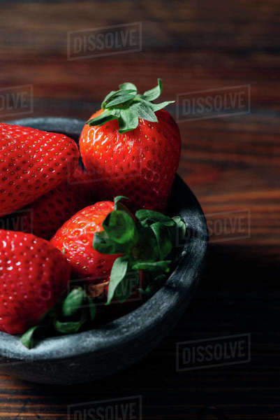 Fresh ripe strawberries in black concrete bowl on wood background ...