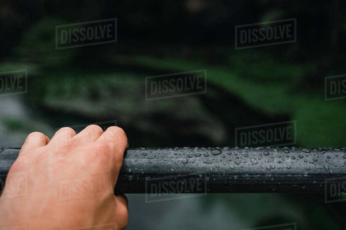 Hand of anonymous person grasping railing with drops of fresh water on ...