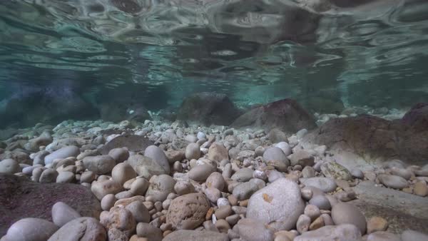 Underwater pebbles and rocks in shallow water with the ripples of water ...