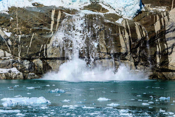 Calving glacier, chunks of ice fall from glacier into Skjoldungen Fjord ...