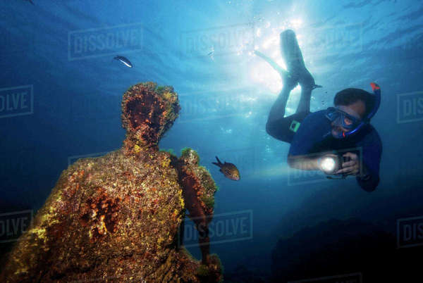 Scuba diver swimming above a submerged ancient Roman statue, underwater ...
