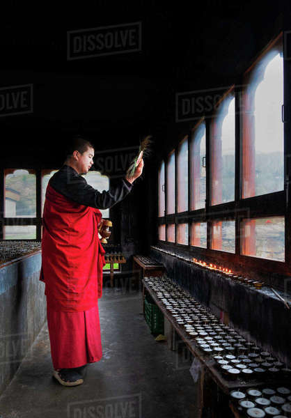 Portrait, Bhutanese Buddhist monk lights candles for worshippers to ...