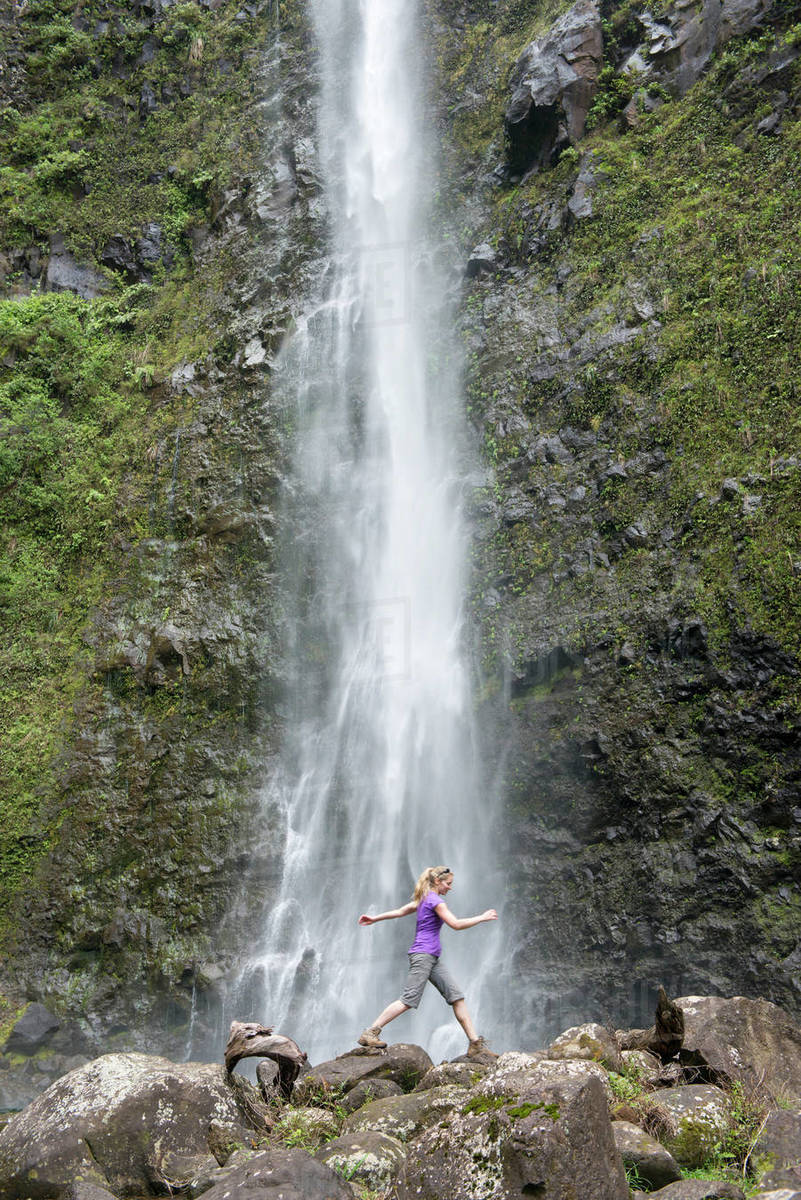 Hiker leaping in front of a waterfall along the famous Kalalau Trail ...
