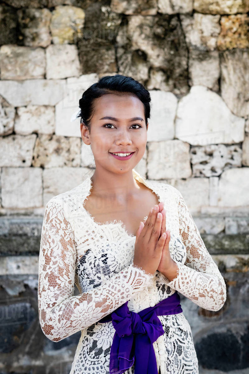 A young Balinese woman in a local temple dress making a formal greeting ...
