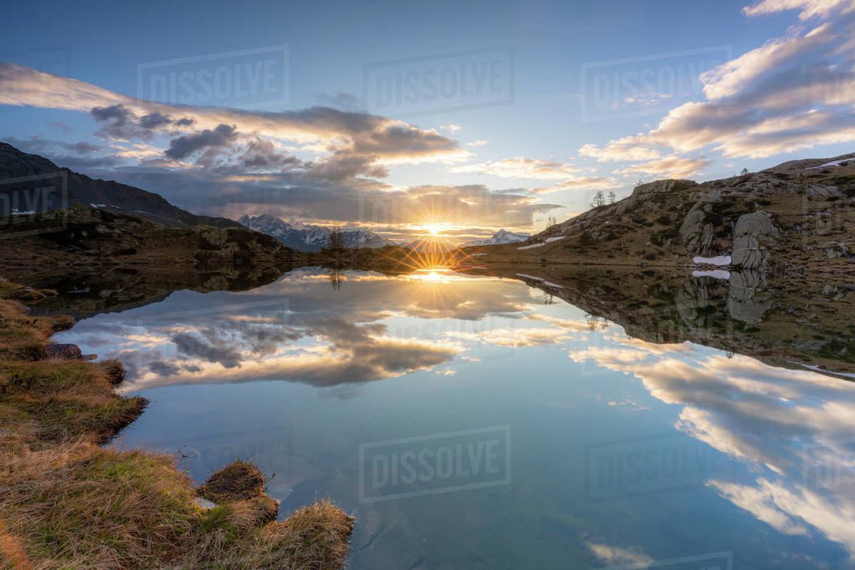 Sunburst over the clear waters of lake Zana during sunrise, Valmalenco ...