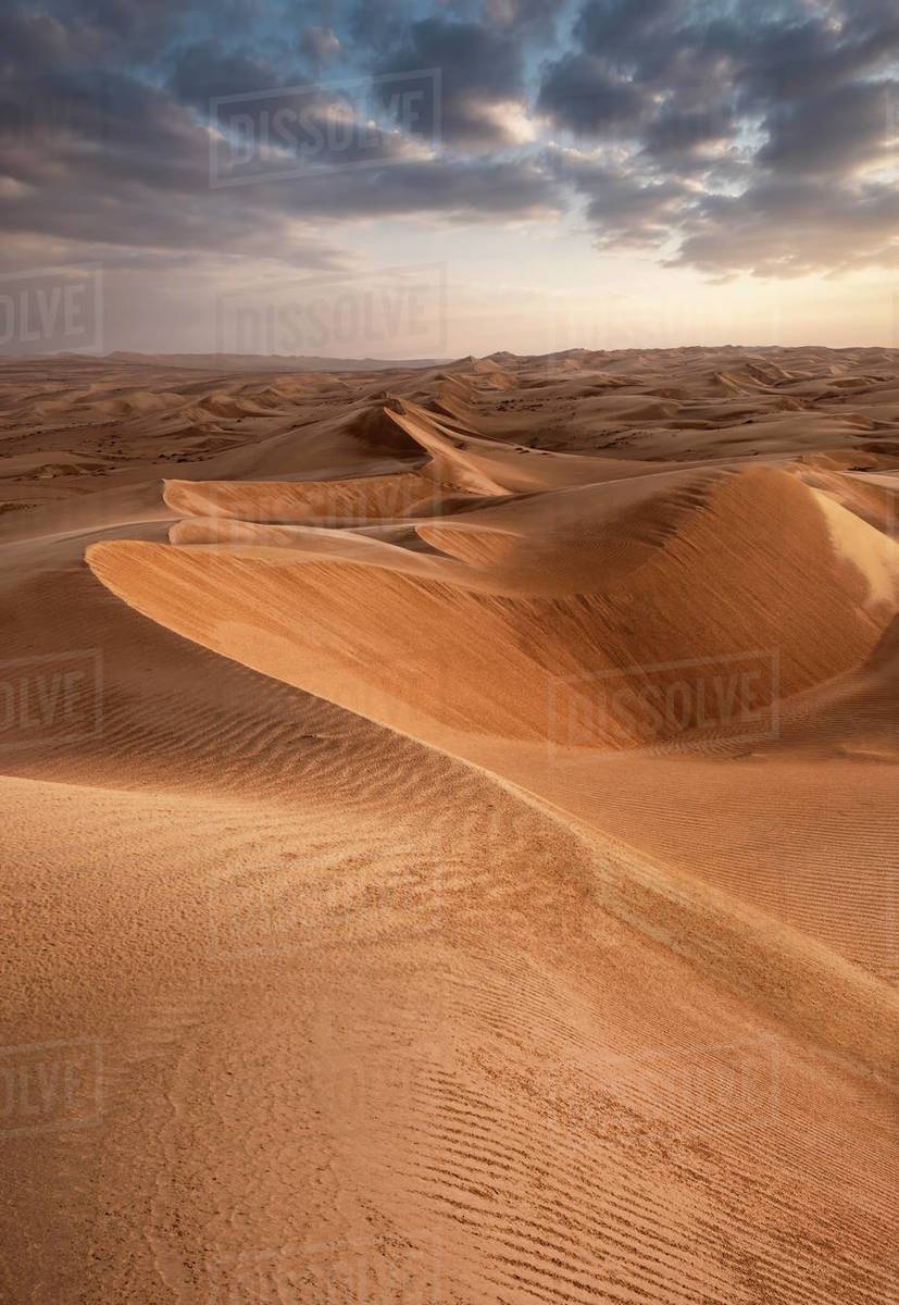 Sand dunes at sunset in the Wahiba Sands desert with clouds in the sky ...