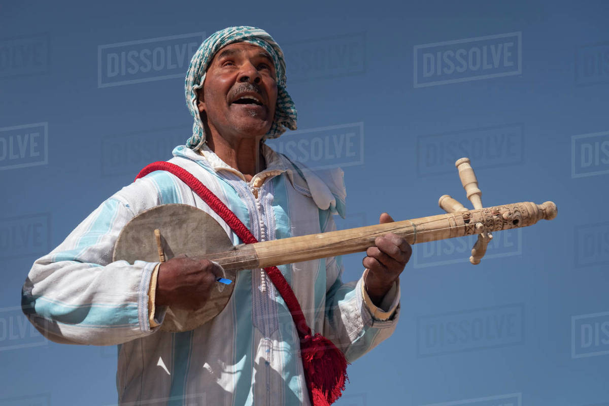 Moroccan man in traditional dress playing a traditional Gimbri ...