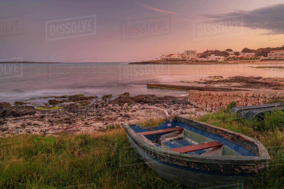 View of Playa Punta Prima and rowing boat at dusk, Punta Prima, Menorca ...