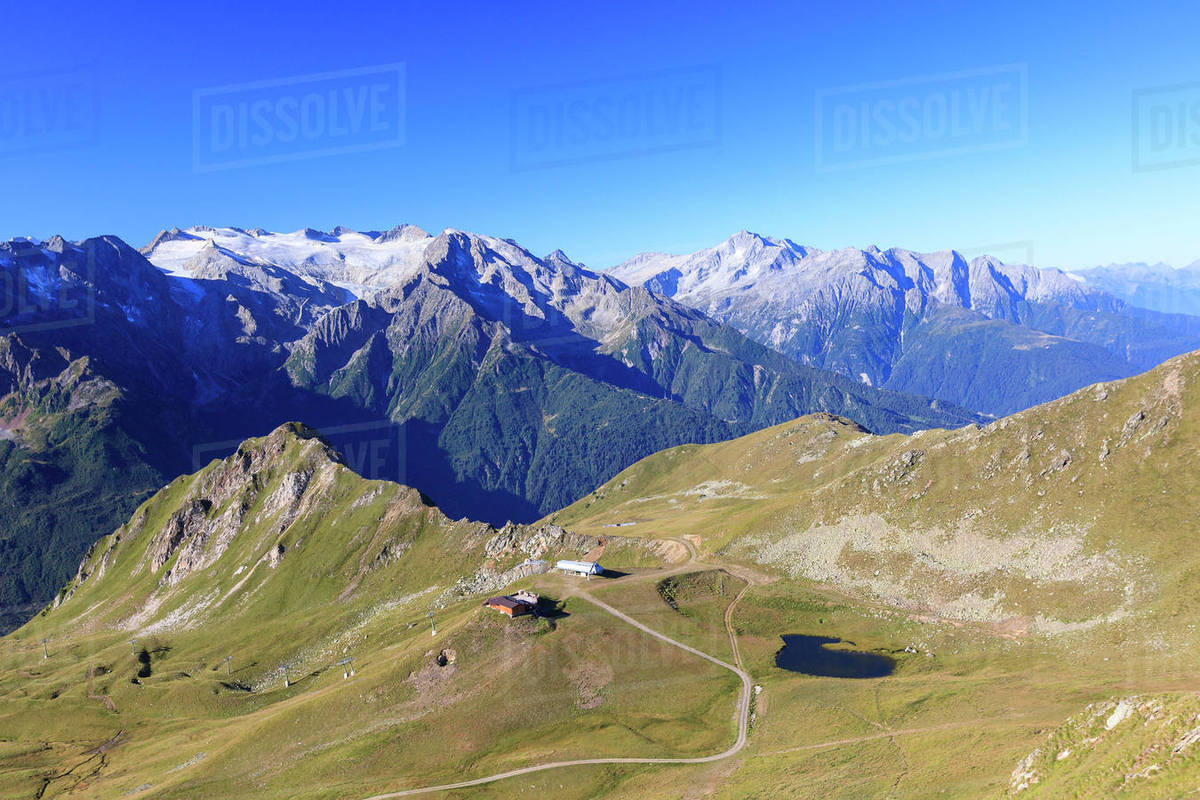 Green meadows and alpine lake framed by the high peaks in the Adamello ...