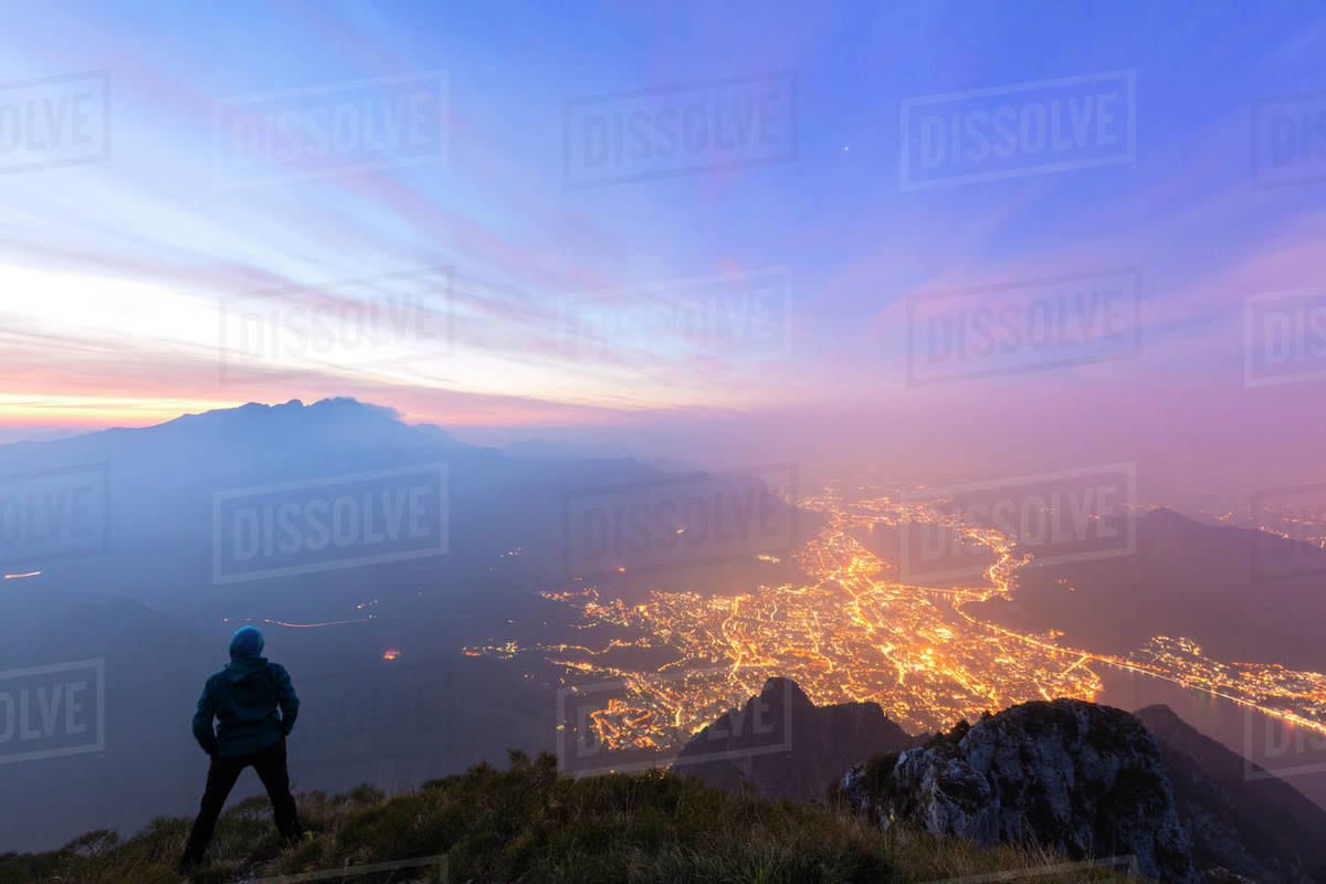 Hiker on Monte Coltignone looks toward Monte Resegone and Lecco at dawn ...