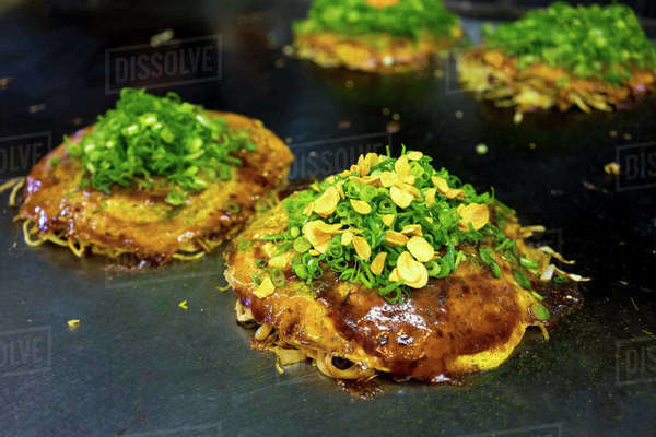 Okonomiyaki, Japanese style savoury pancakes, on a large griddle in a ...