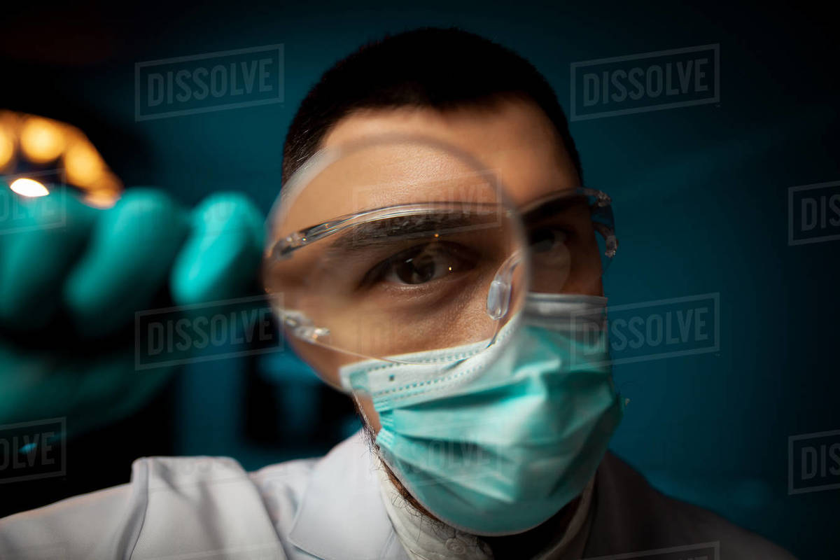 Man in blue protective mask hilding magnifying glass on dark blue ...