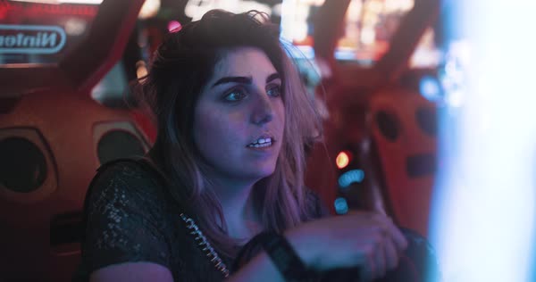 Girl is driving a race car game at the arcade with flashing neon lights ...