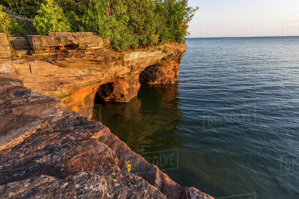 Layered sandstone cliffs and sea caves at sunrise on Devils Island in ...