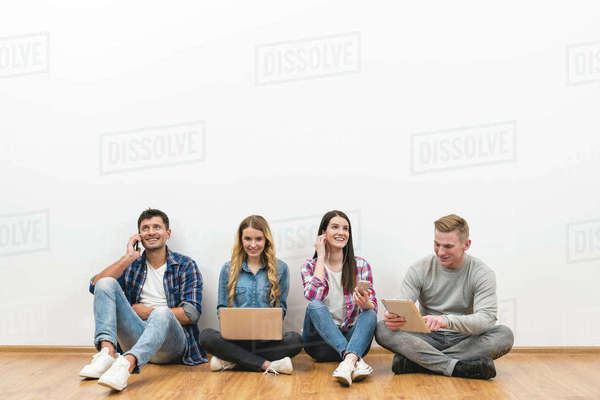 The four friends with gadgets sit on the floor on the white wall ...