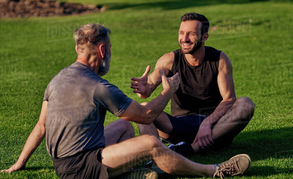 The two happy men sitting on the grass and handshaking - Royalty-free ...