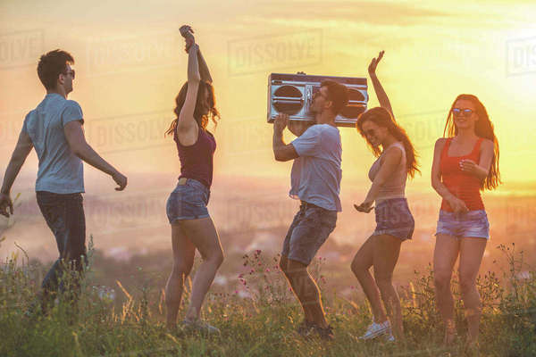 The five happy people dancing with a boom box on the sunset background ...