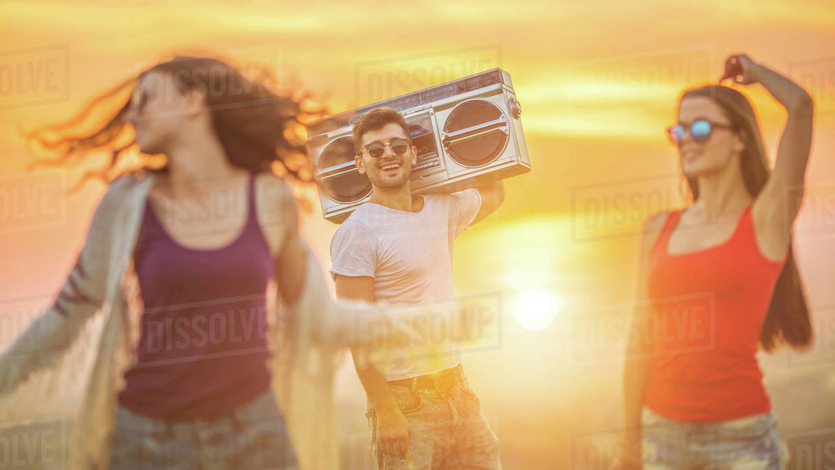 The happy people with a boom box fun in the background of the sunset ...