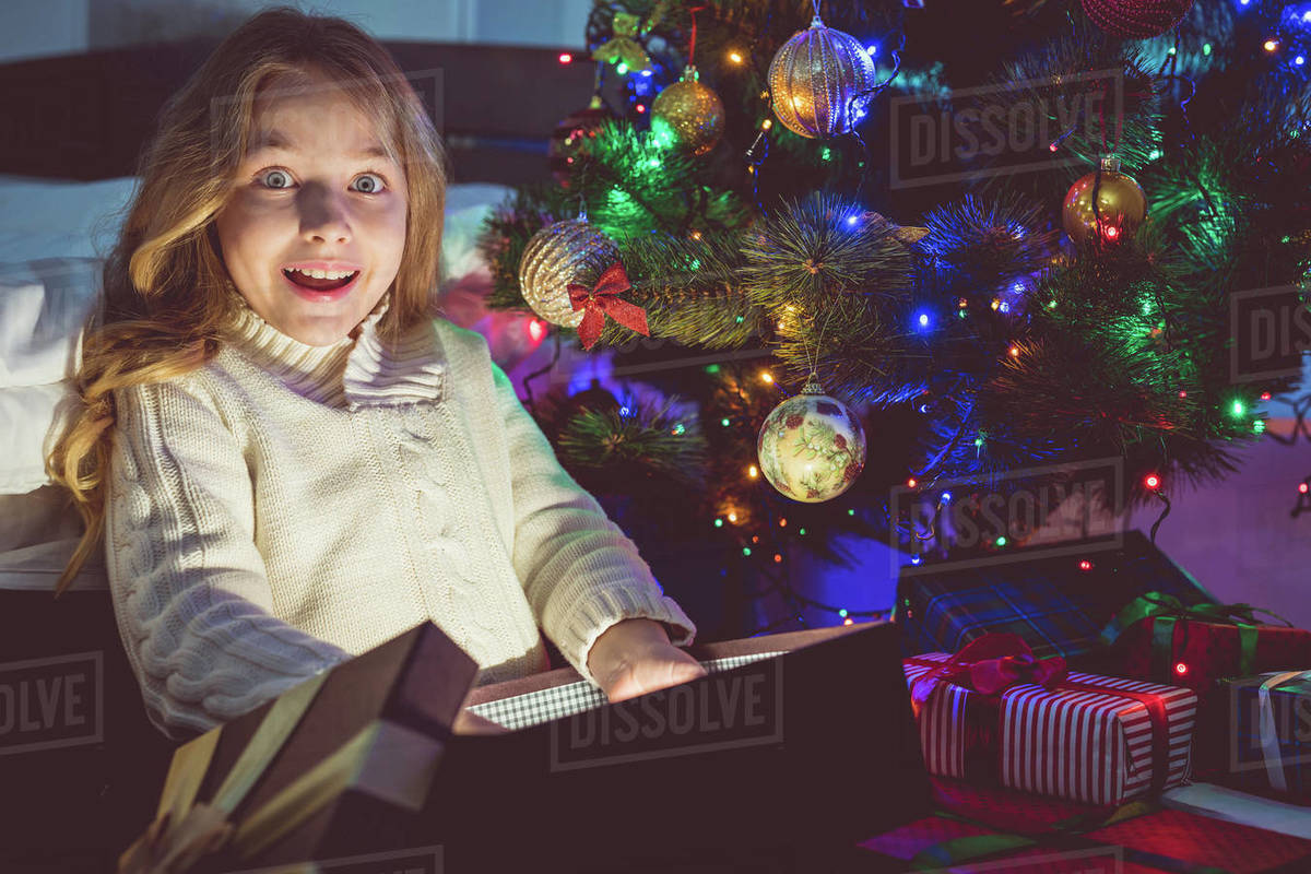 The girl unpack the gift on the christmas tree background. evening ...