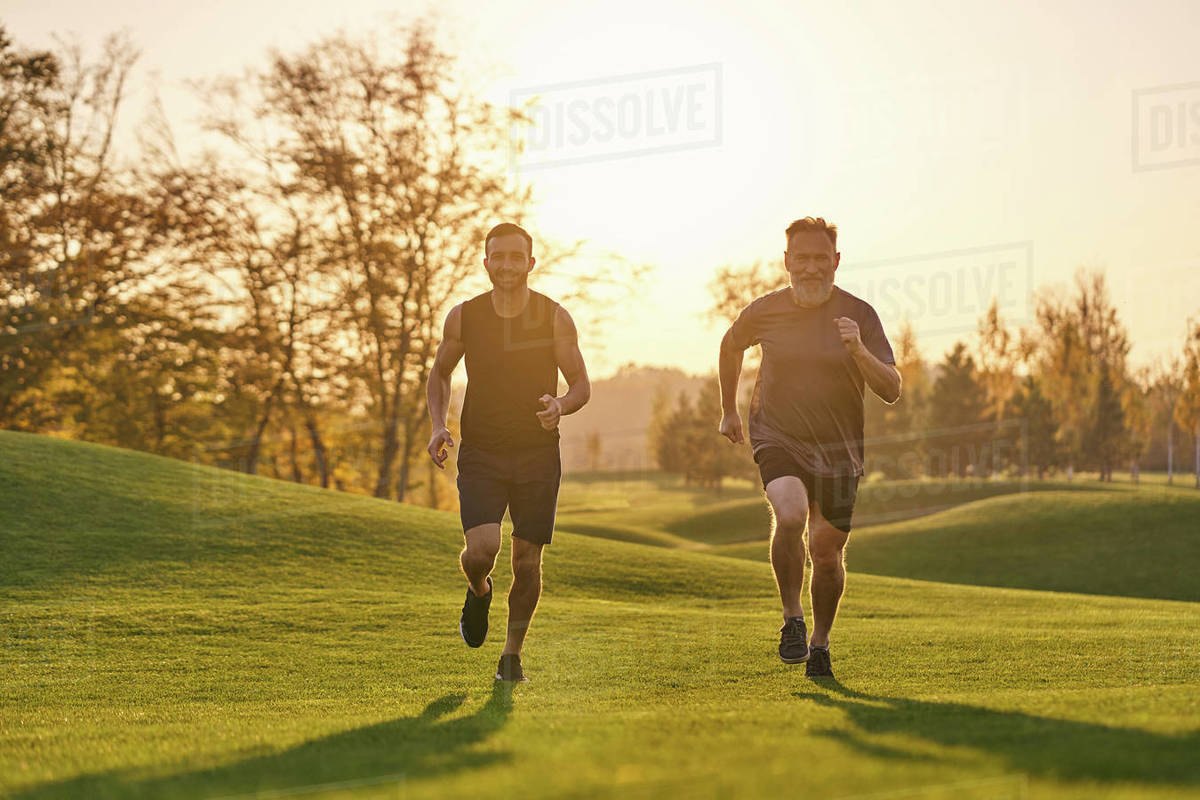 The father and son running in the beautiful park on the sunset ...