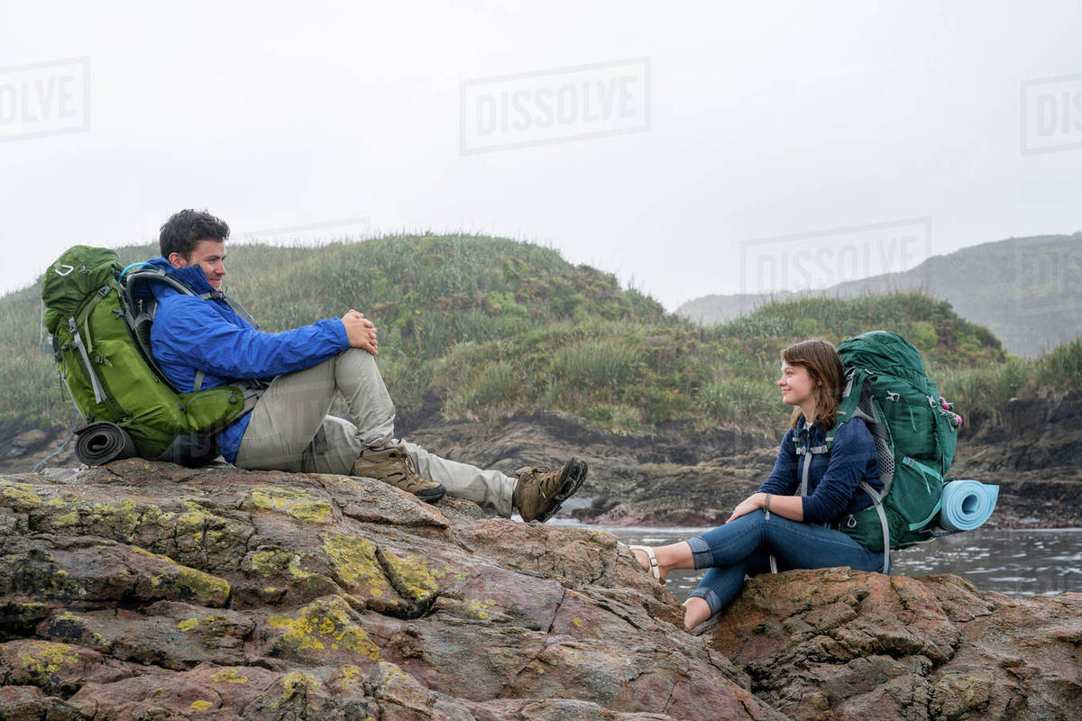 Young couple with backpack, sitting on rocks, Constant Bay, Charleston ...