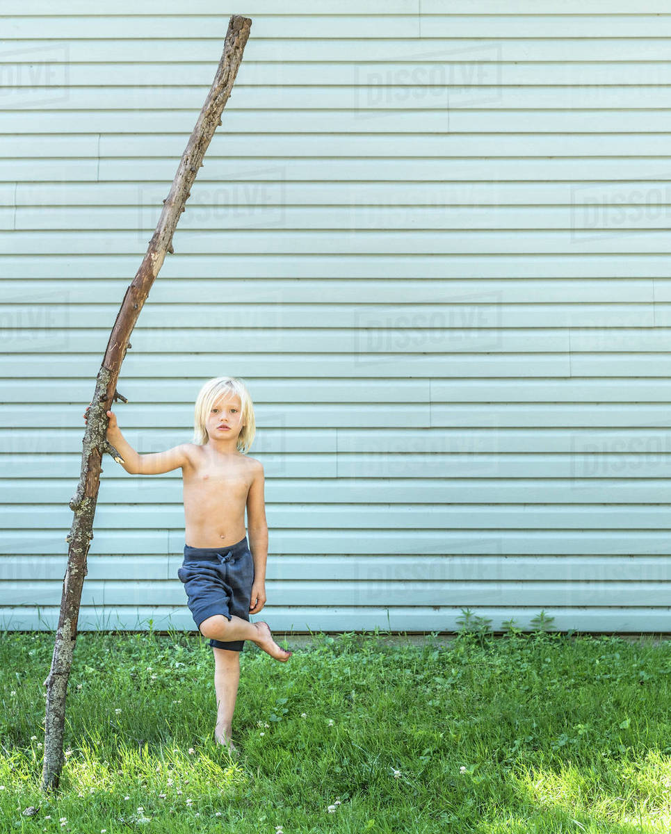 Boy standing on one leg holding stick - Stock Photo - Dissolve