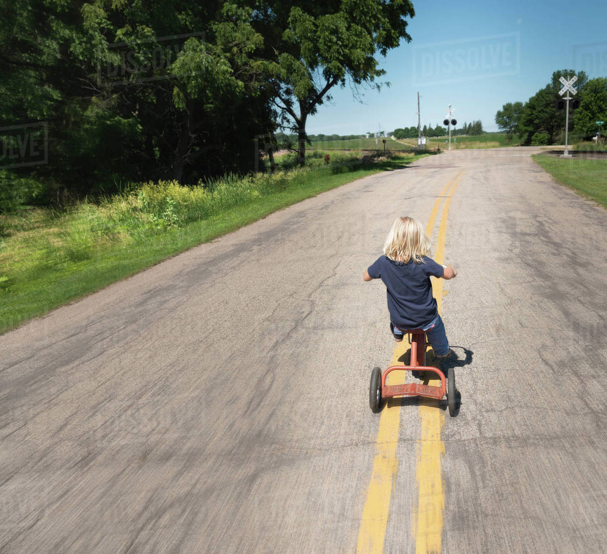 Rear view of boy riding bicycle on road - Stock Photo - Dissolve