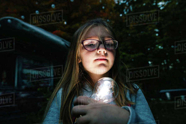 Portrait of girl holding illuminated lightbulb in garden at dusk ...