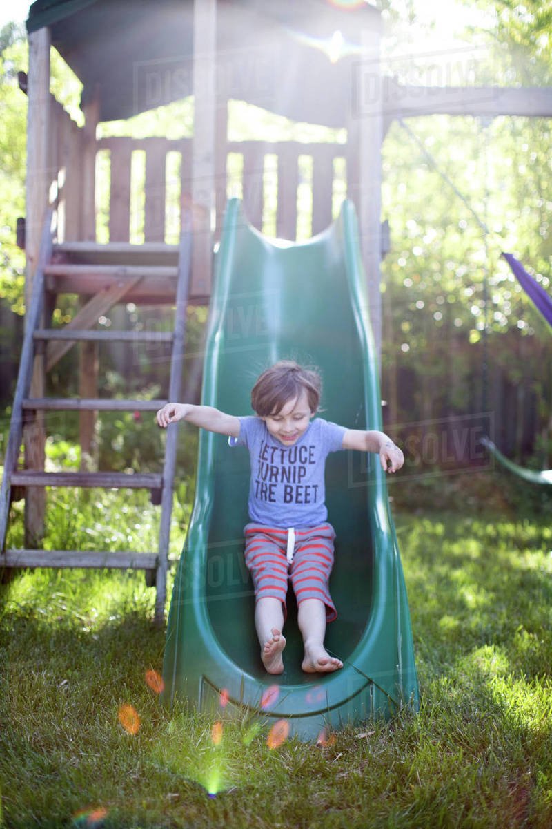 Boy sliding down garden slide - Stock Photo - Dissolve