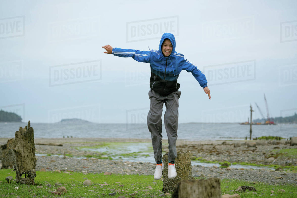 Teenage boy jumping from tree stump, Pacific Rim National Park ...