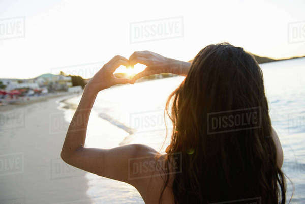Woman making heart shape around sun - Stock Photo - Dissolve