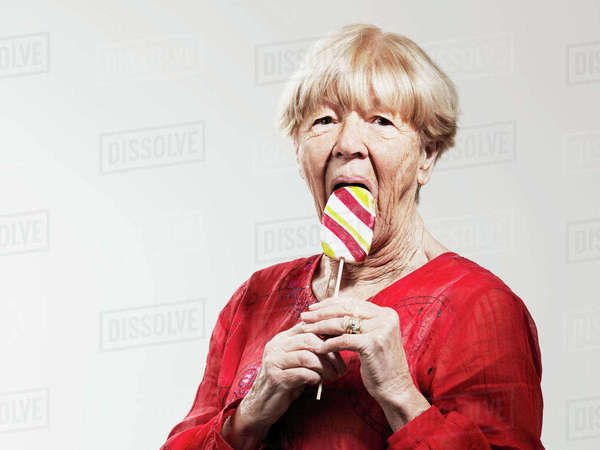 Senior woman eating lollipop against white background - Stock Photo ...