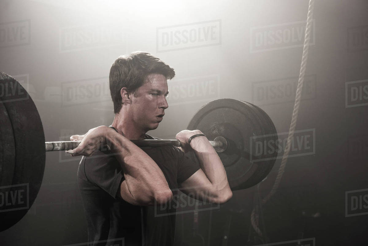 Young man lifting barbell - Stock Photo - Dissolve