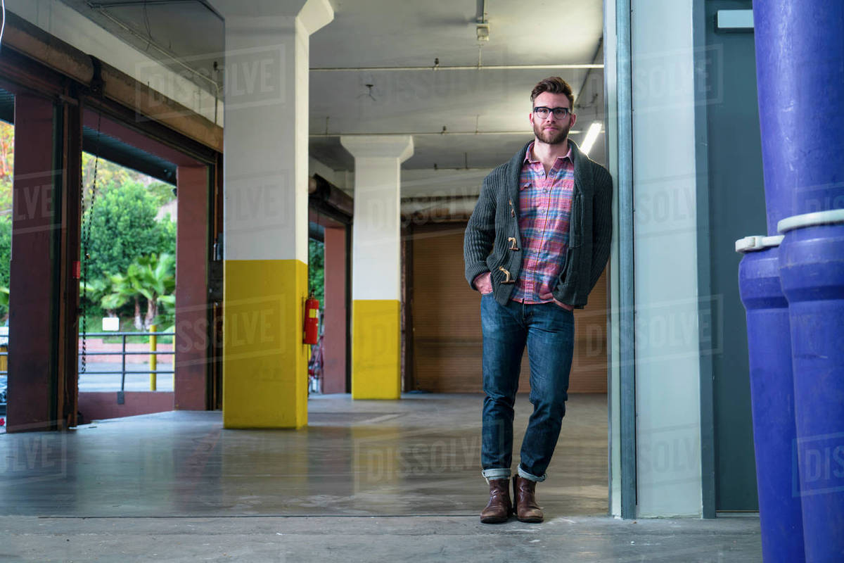 Young man in lobby leaning against wall, hands in pockets, looking at ...