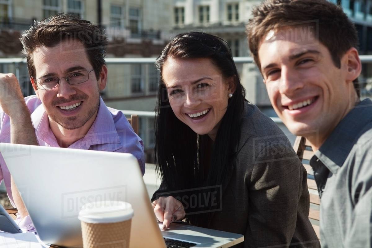 Three people smiling at the camera while using a laptop - Royalty-free ...