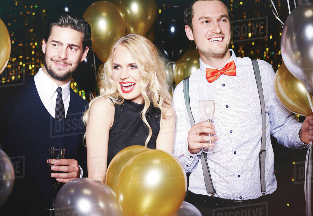 Portrait of three people at party, surrounded by balloons, holding ...