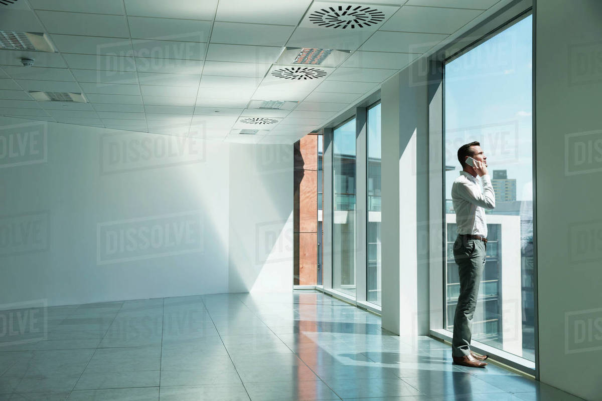 Businessman, looking out of window in empty office space, using ...