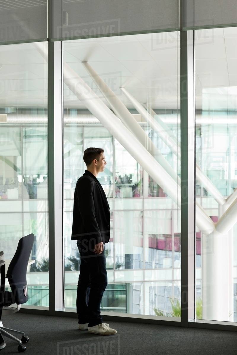 Young man looking out of window in IT office - Stock Photo - Dissolve