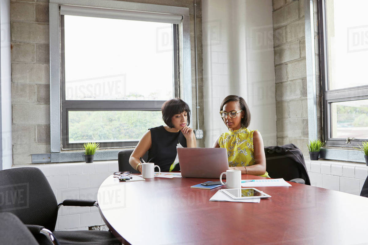 Two women sitting at meeting room table, using laptop - Royalty-free ...