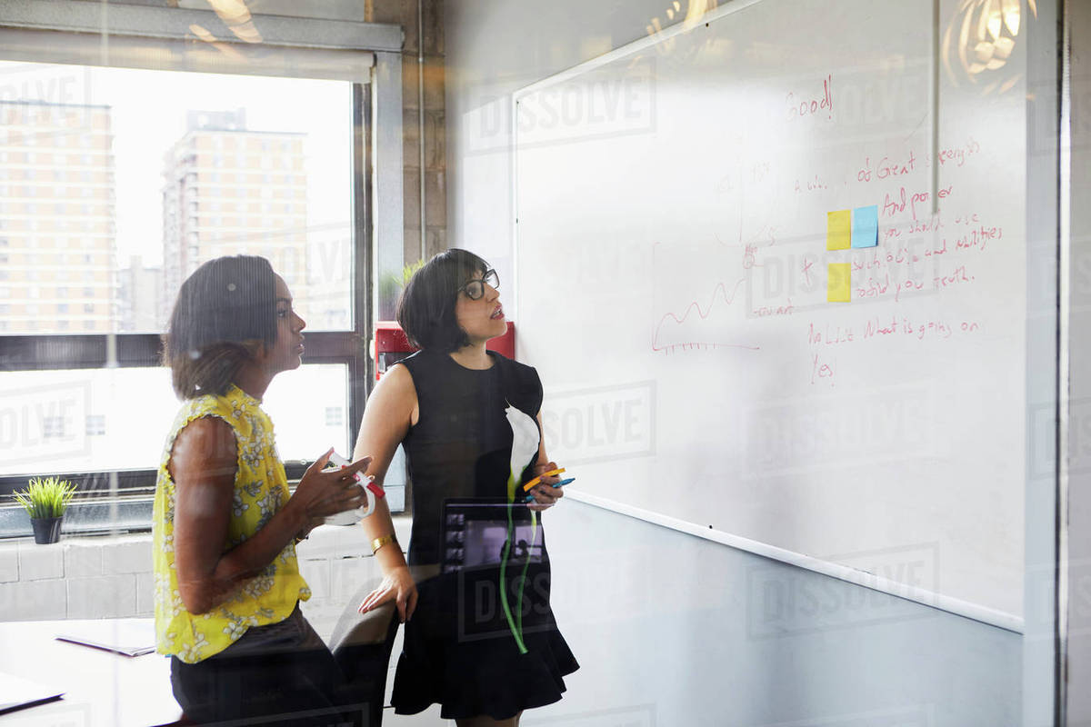 Two women in office, solving problem, using whiteboard, sticky notes ...