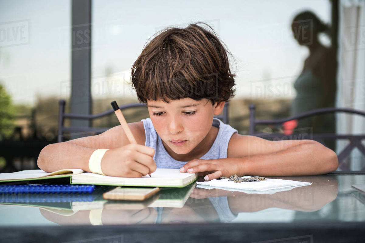 Boy at table writing in workbook - Royalty-free Stock Photo | Dissolve