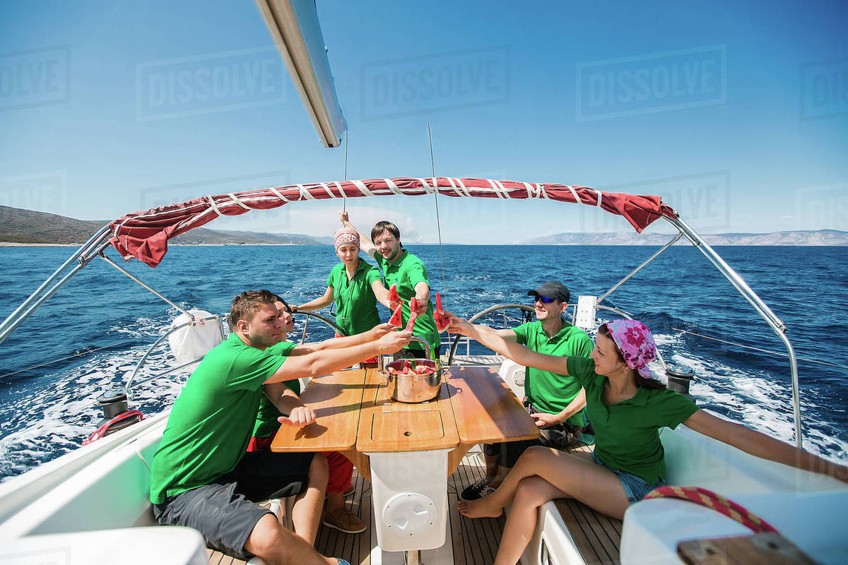 Men And Young Women On Board Yacht Raising A Toast With Sliced Water