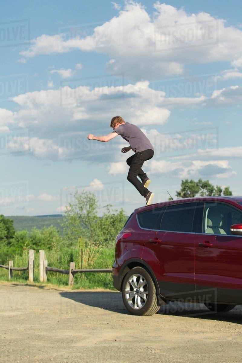 Young man jumping off car - Royalty-free Stock Photo | Dissolve