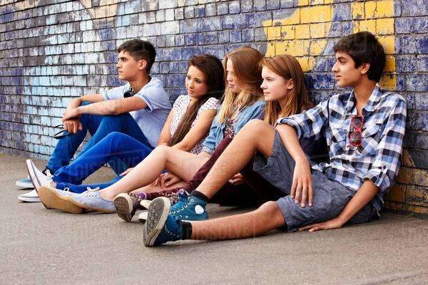 Teenagers sitting against a wall - Royalty-free Stock Photo | Dissolve